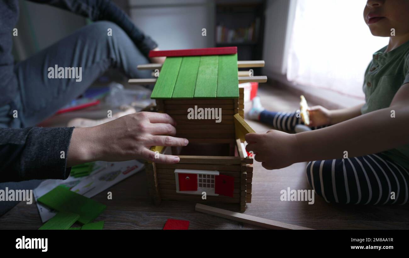 Child playing in room with mother building traditional wooden home toy ...