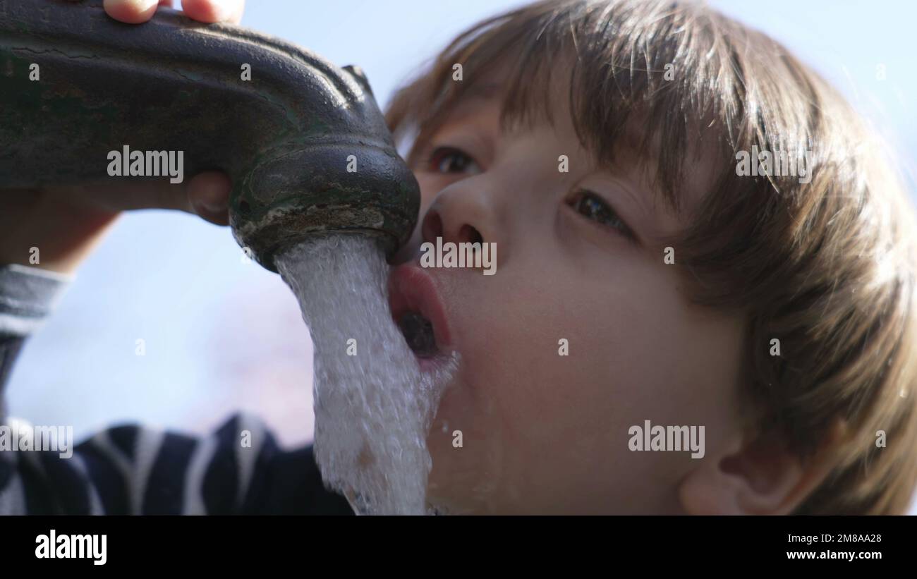 Child drinking water from public faucet outdoors. One little boy ...