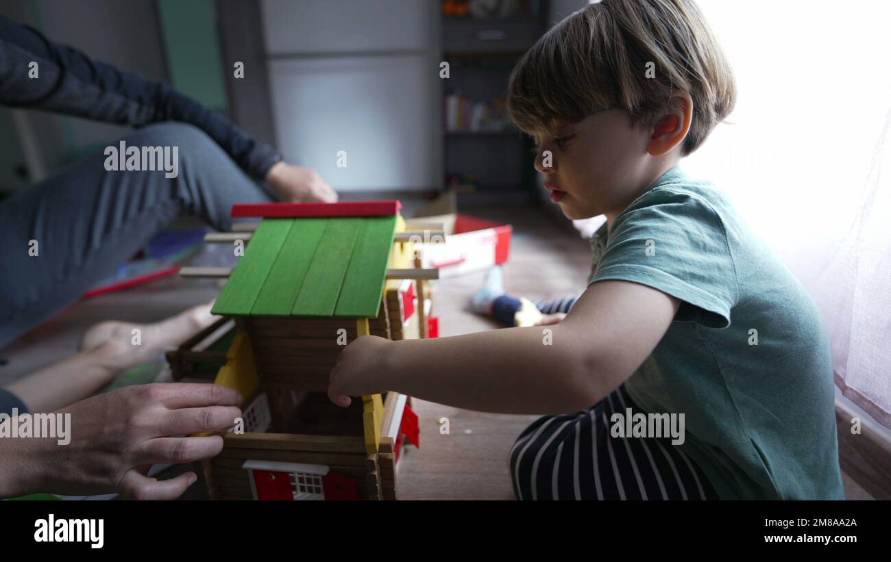 Child playing in room with mother building traditional wooden home toy ...