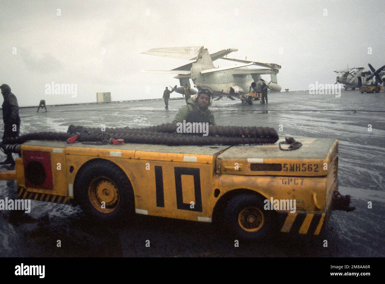 An aircraft handler sits in an MD-3A tow tractor on the flight deck of ...