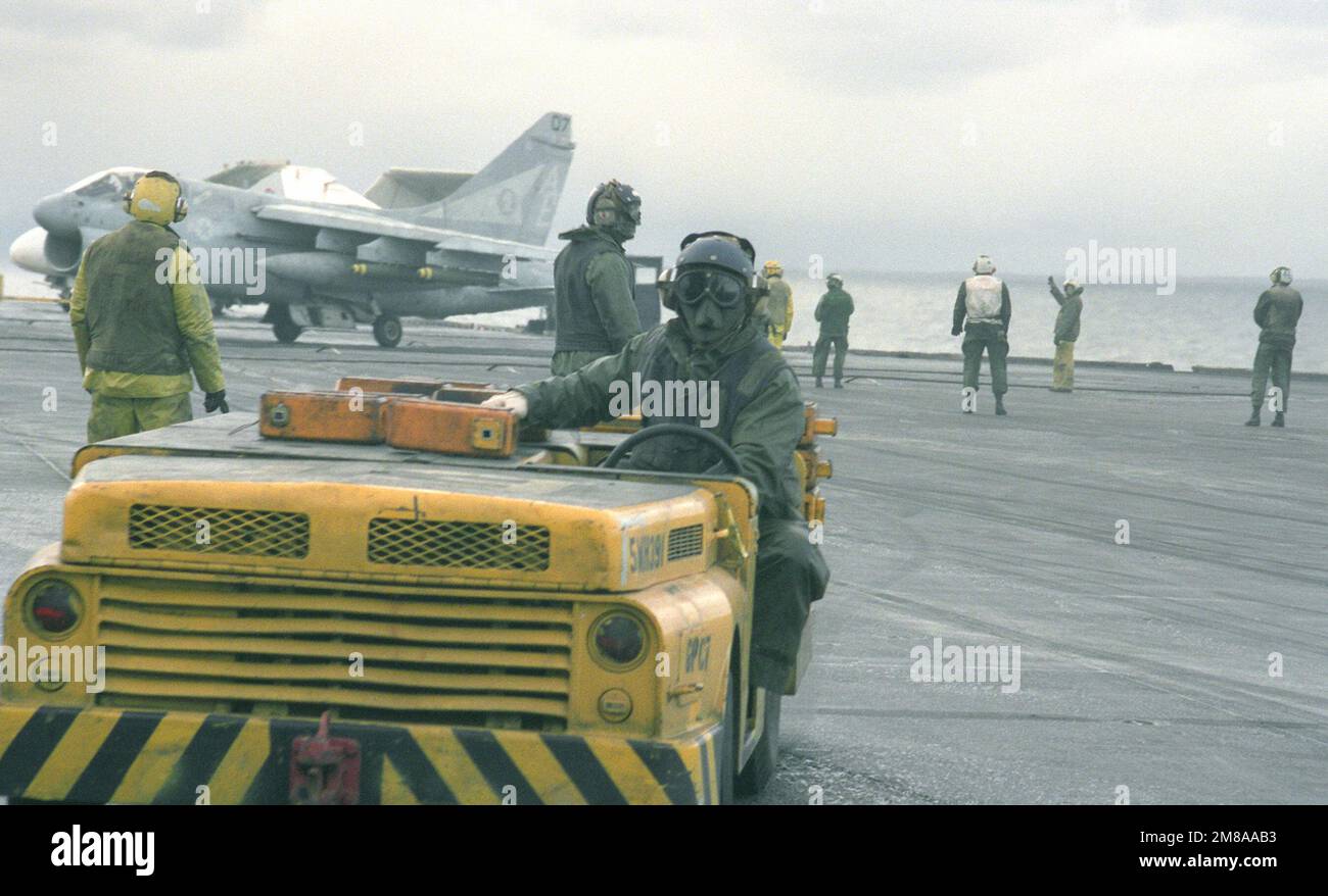 An aircraft handler drives an MD-3A tow tractor across the flight deck ...