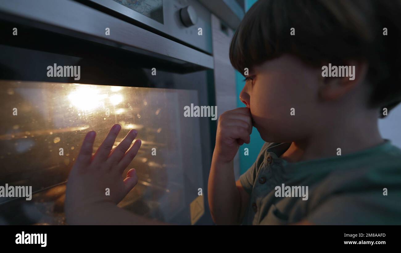 Child staring at oven. Kid looking at cookies baking inside heating ...