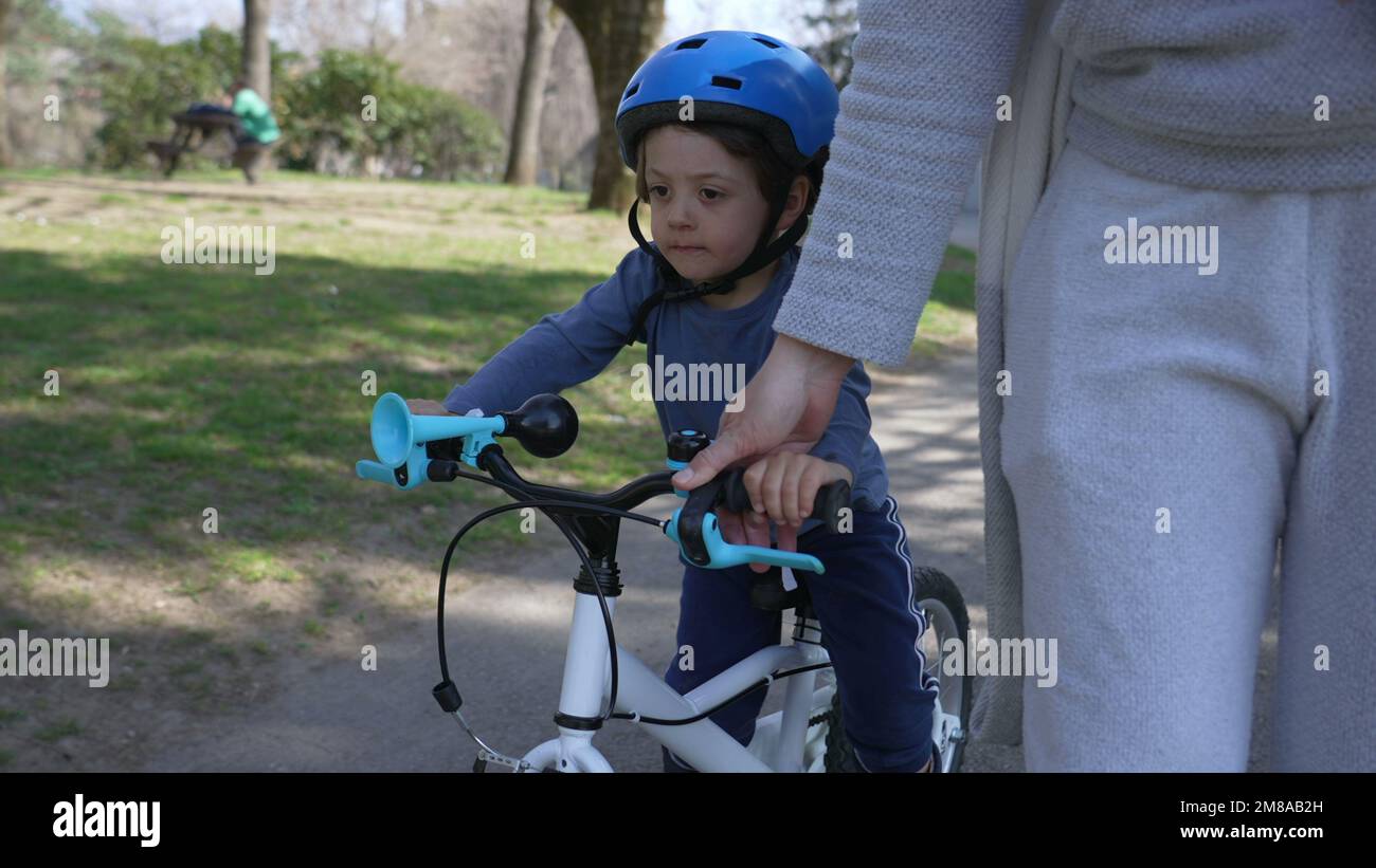 Little boy learning to ride bicycle with mother support. Mom helping ...