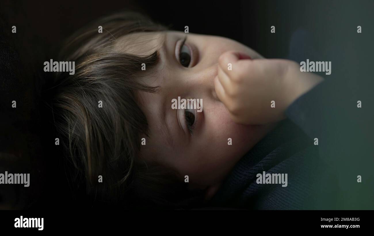 One bored little boy lying on sofa hypnotized by content online watching cartoons. Sleepy child ...