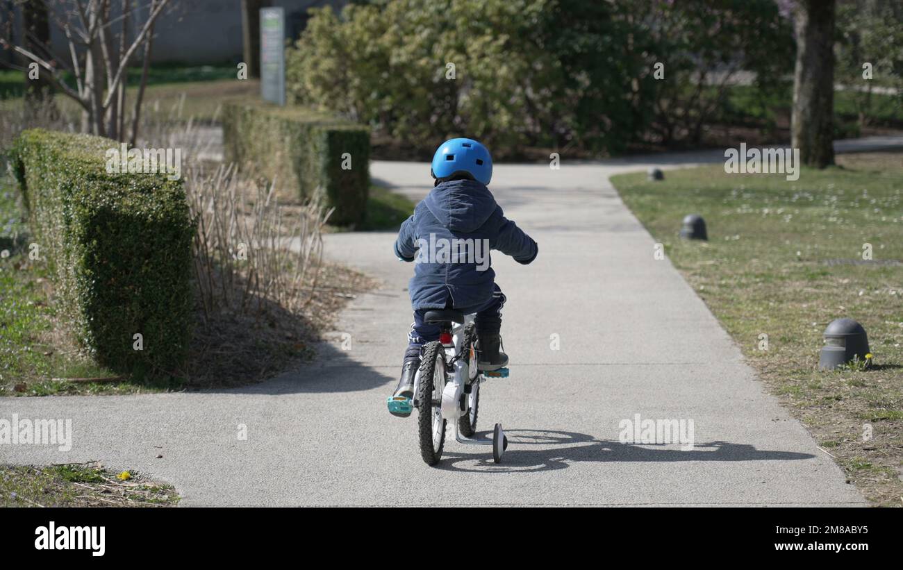 Back of child riding bicycle outdoors wearing helmet. One little boy ...
