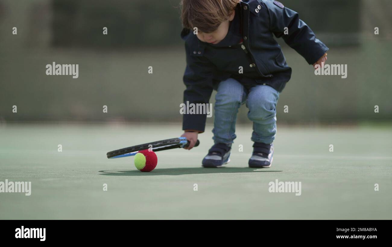 Child stopping tennis ball with racket outdoors wearing winter coat ...