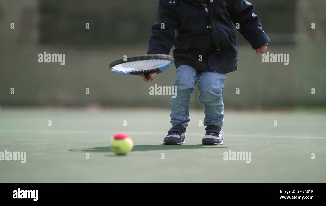 Child stopping tennis ball with racket outdoors wearing winter coat ...