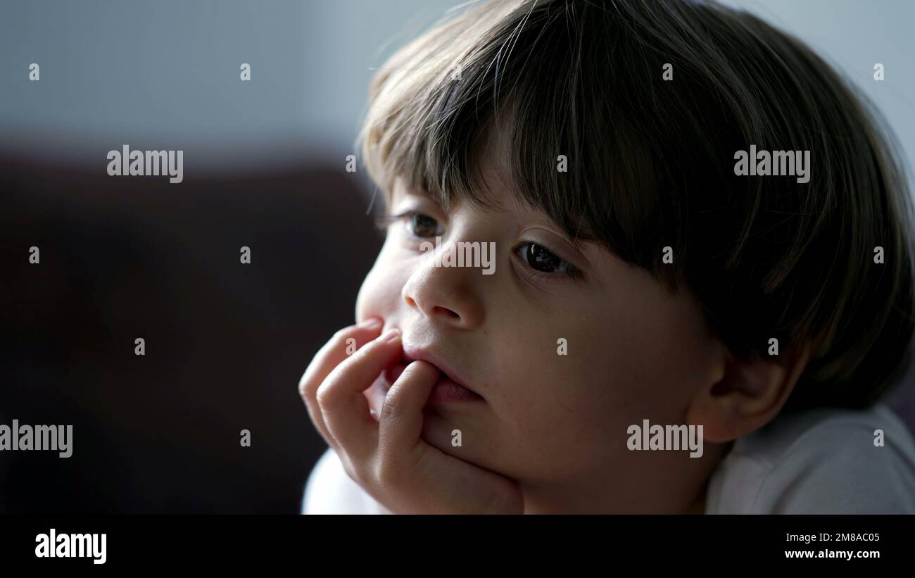 One small boy closeup face with hand in chin watching screen off camera ...