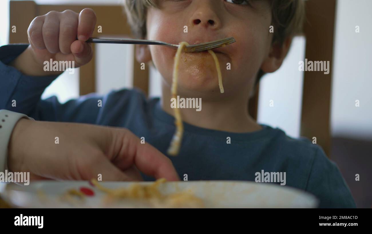 Closeup child face eating pasta. One blond make kids eats noodles ...