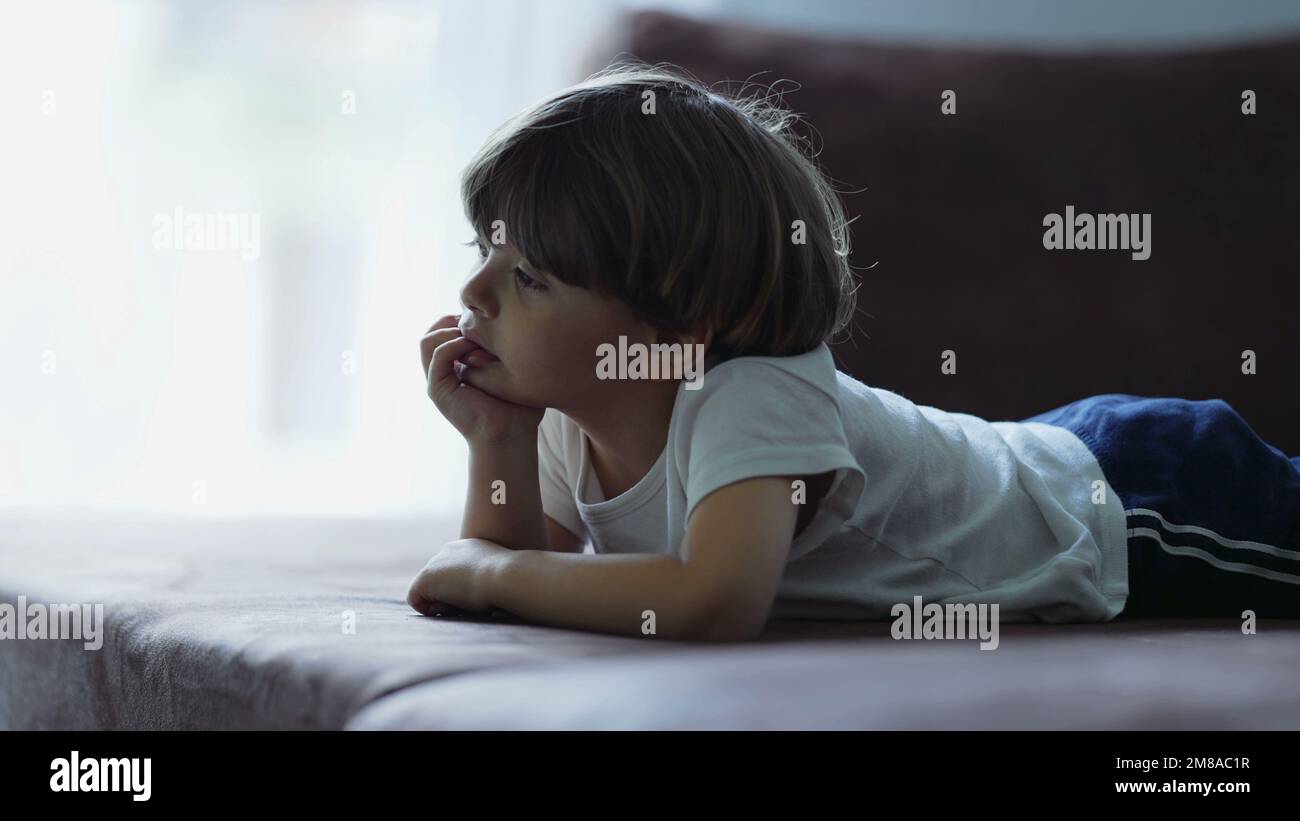 One small boy closeup face with hand in chin watching screen off camera ...