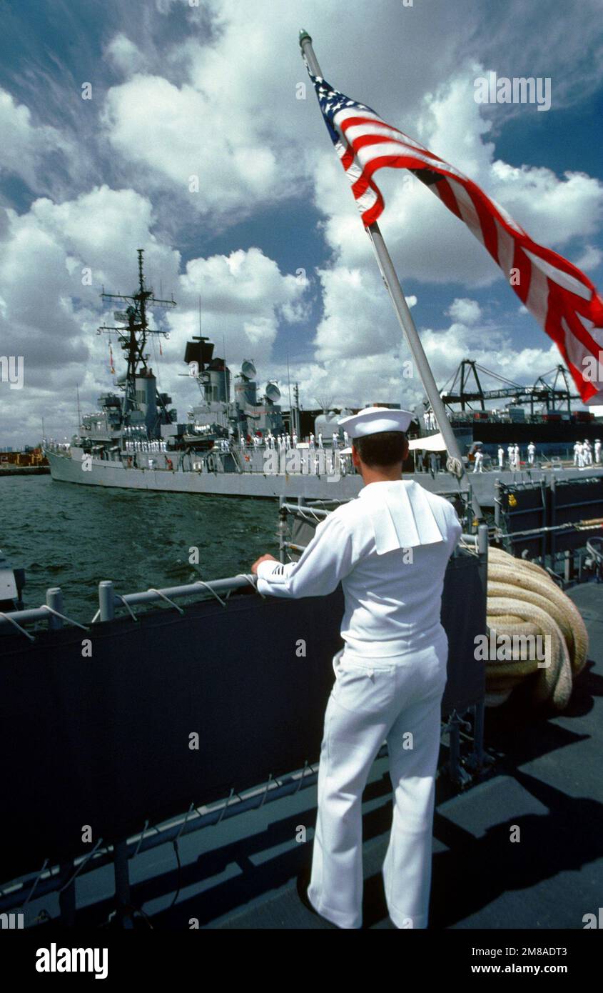 A sailor looks over the railing at the guided missile destroyer USS ...