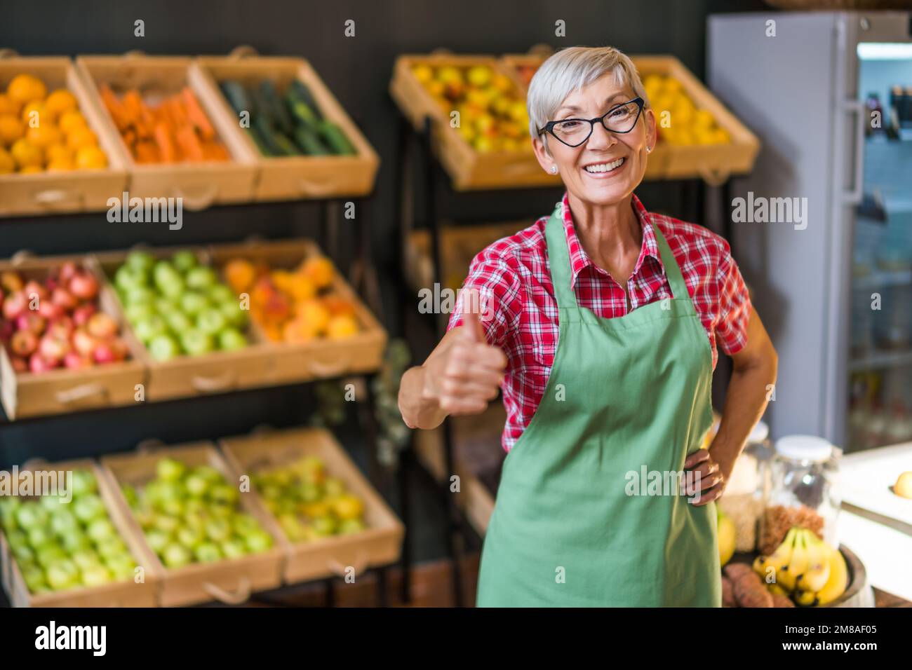 Mature woman works in fruits and vegetables shop. Portrait of small ...