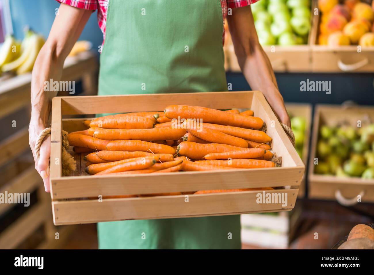 Worker in fruits and vegetables shop is basket with carrots Stock Photo ...