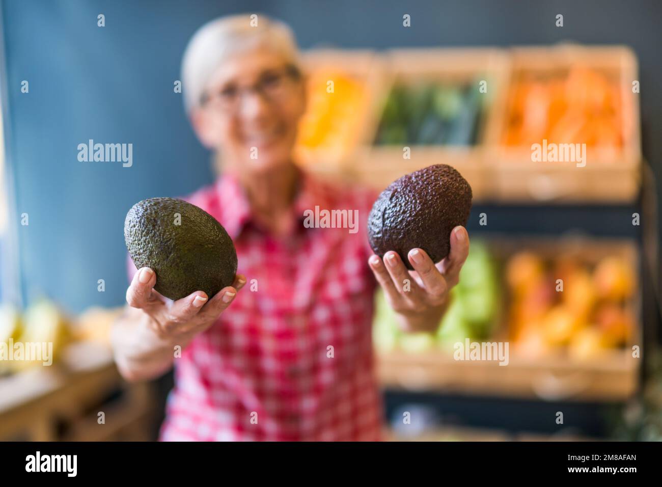 Worker in fruits and vegetables shop is holding avocado. Close up of ...