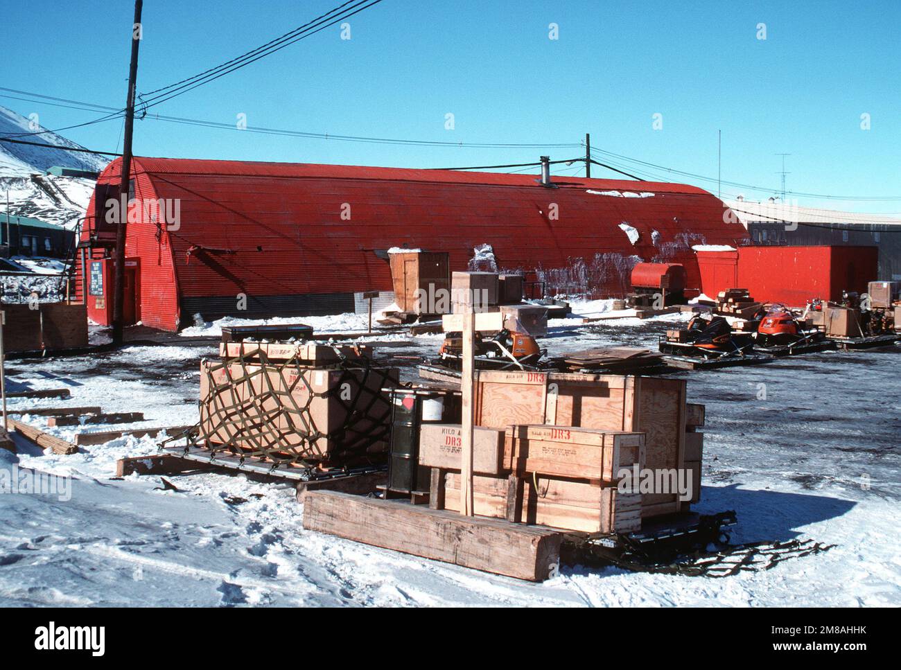 Crates, snowmobiles and 55-gallon drums sit on pallets in a storage lot ...