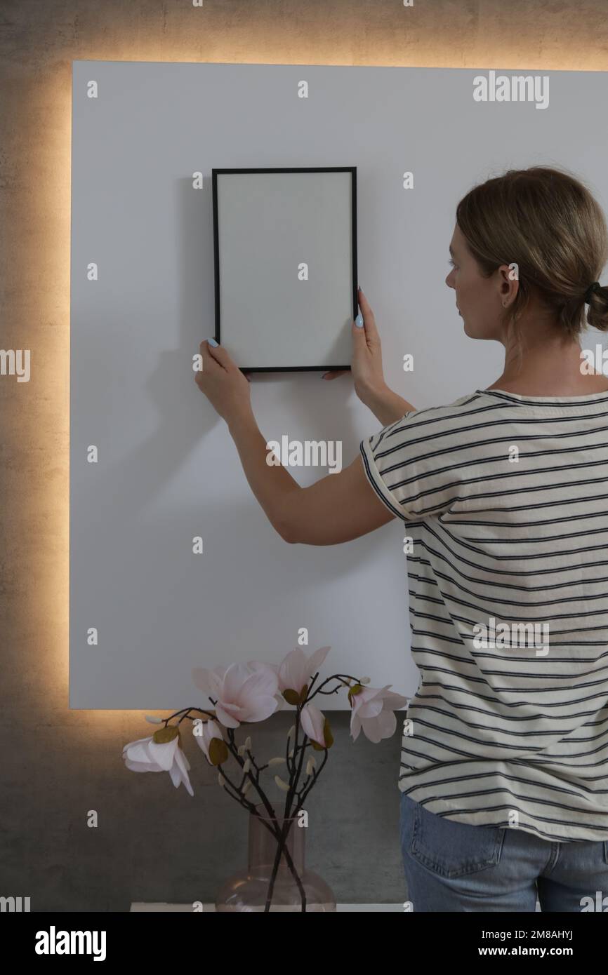 Woman arranging picture frames on wall in new house, diy home ...