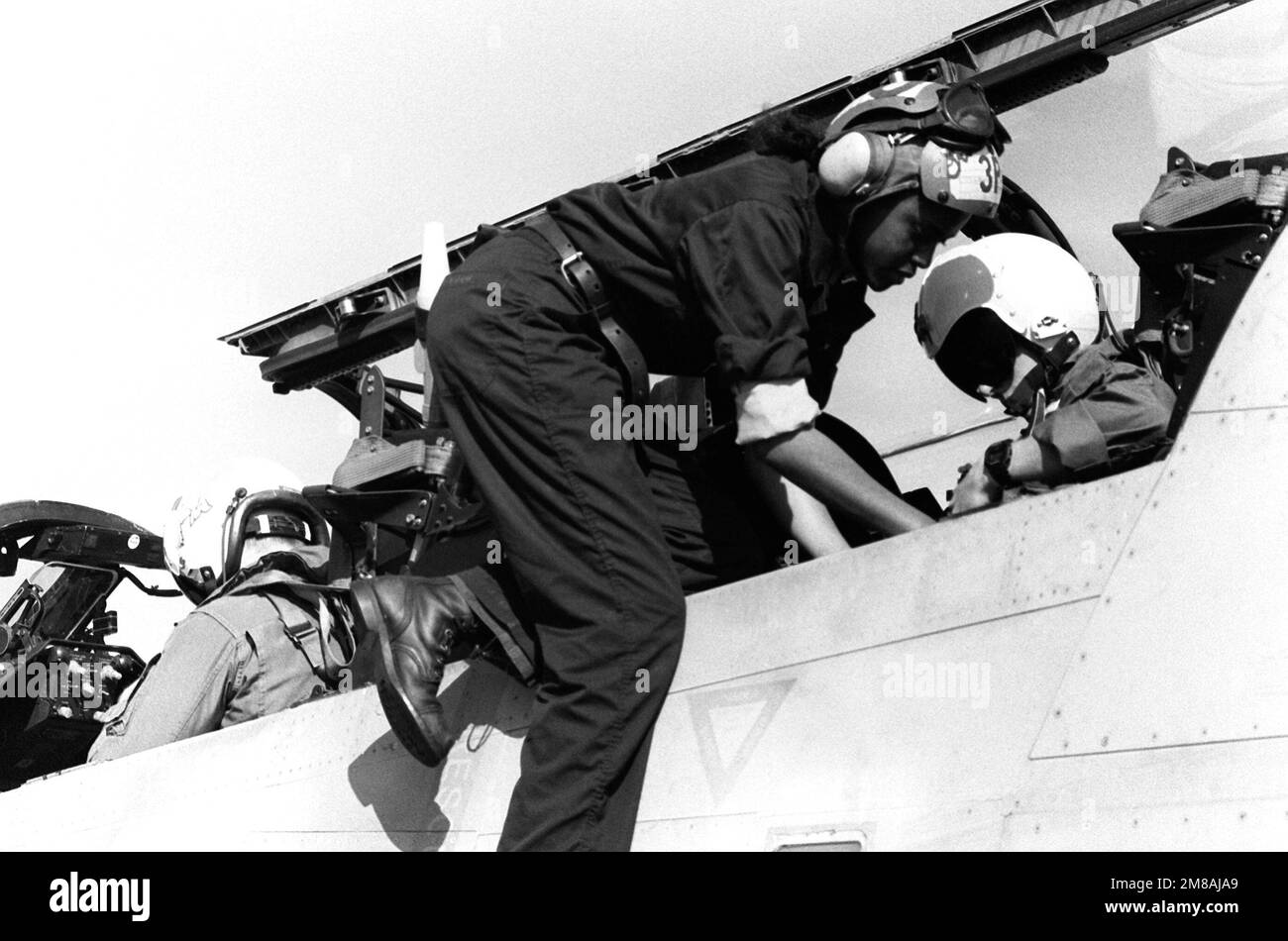 AIRMAN Ora Howard, plane captain, helps secure a pilot into the cockpit ...