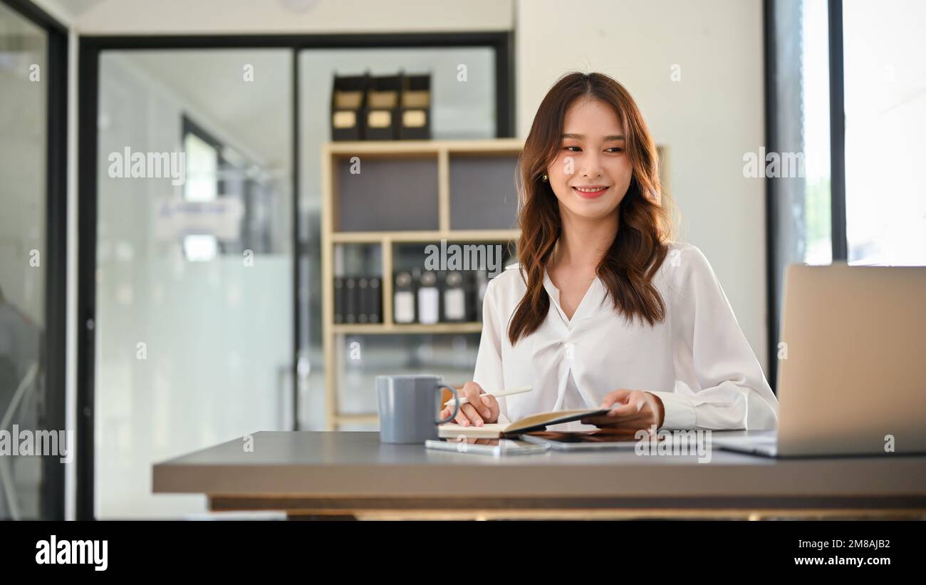 Beautiful and happy millennial Asian businesswoman working at her desk ...