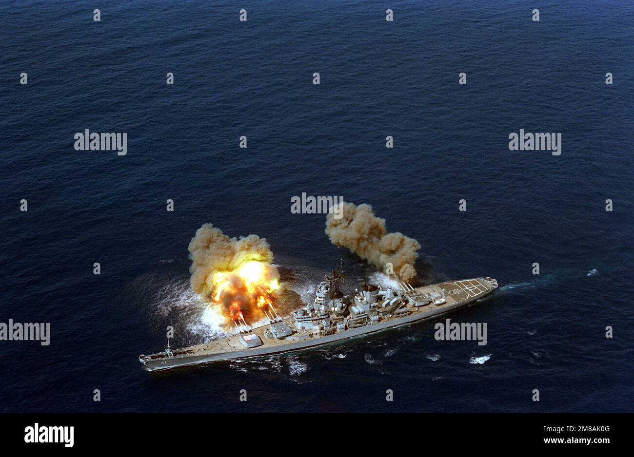 An aerial view of the battleship USS IOWA (BB-61) firing its Mark 7 16-inch 50-caliber guns to ...