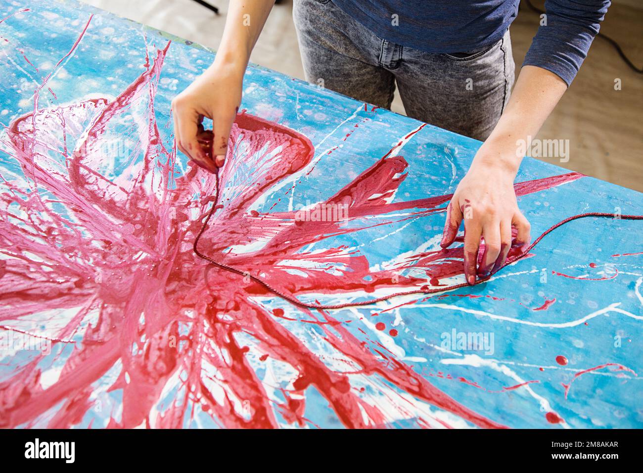 Top view of hands of woman stained with red paint painting with rope ...