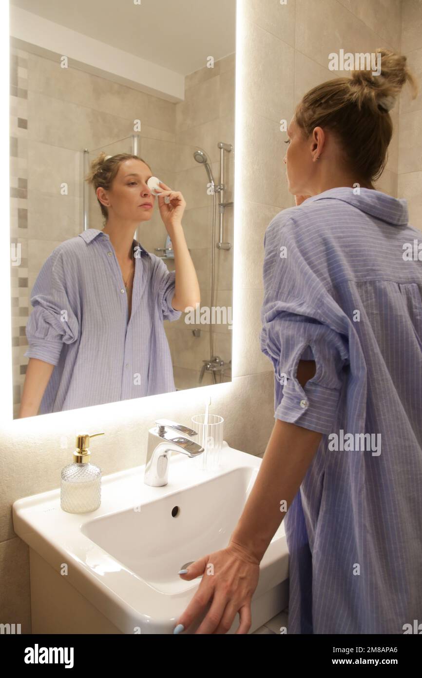 Young woman doing her morning or evening routine in the front of mirror ...