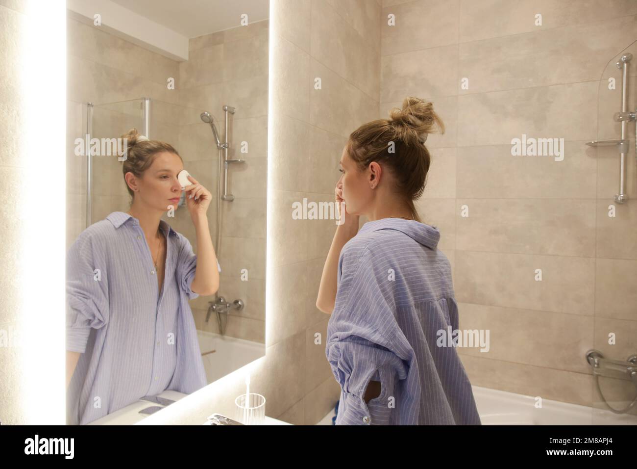 Young woman doing her morning or evening routine in the front of mirror ...