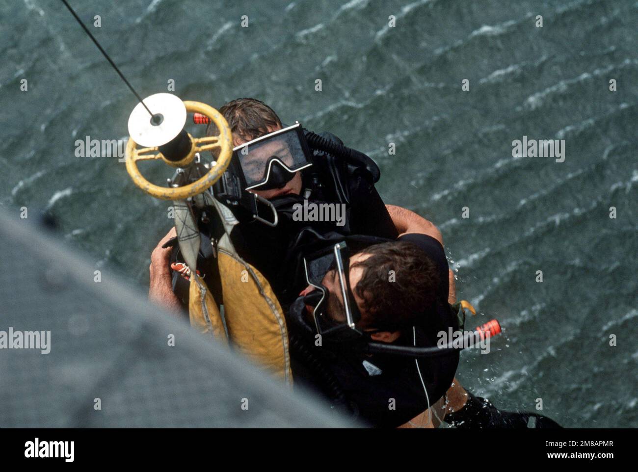 Two search and rescue (SAR) swimmers are winched from the water by a ...