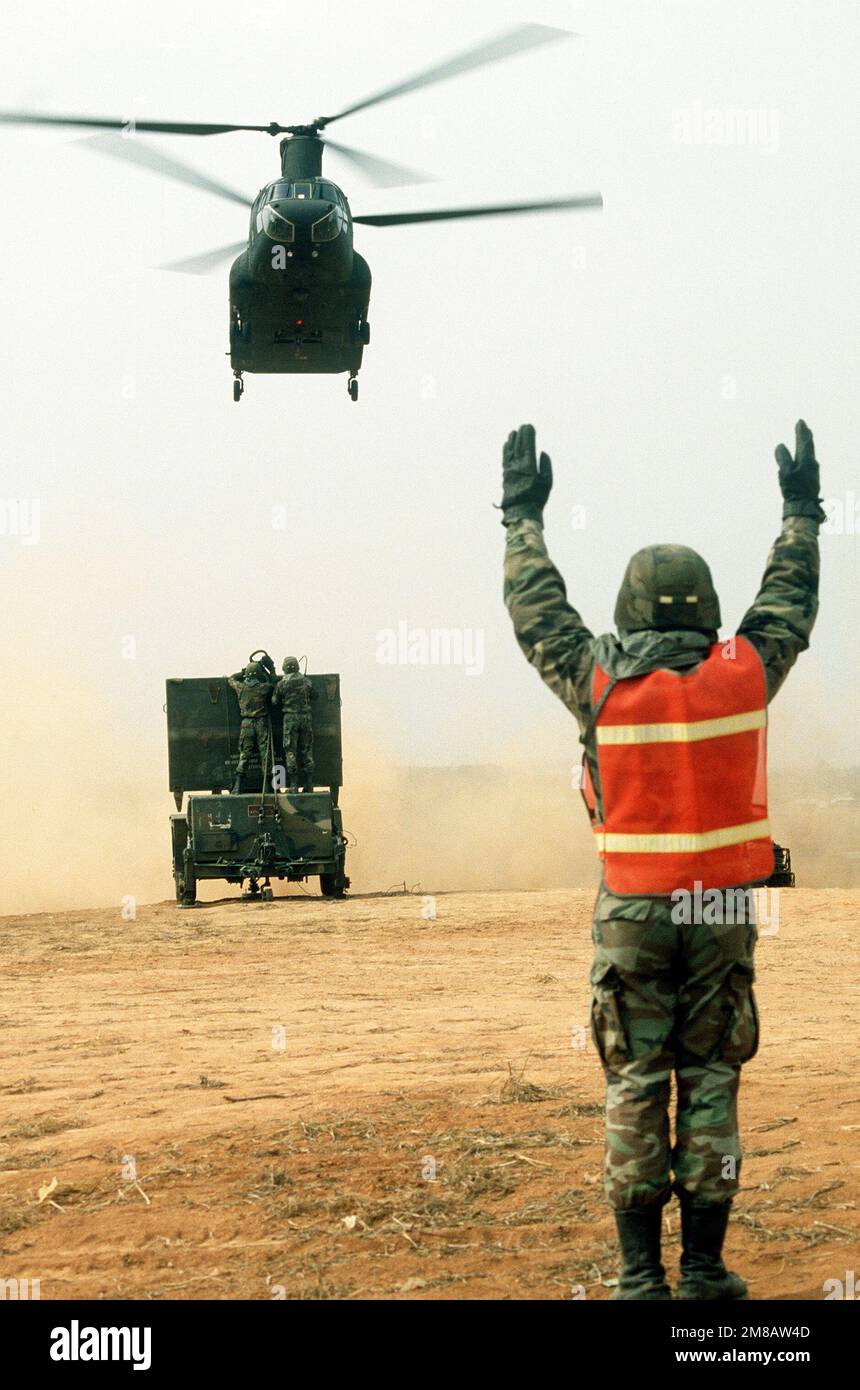 A member of the ground support crew signals to the pilot of a CH-47 ...