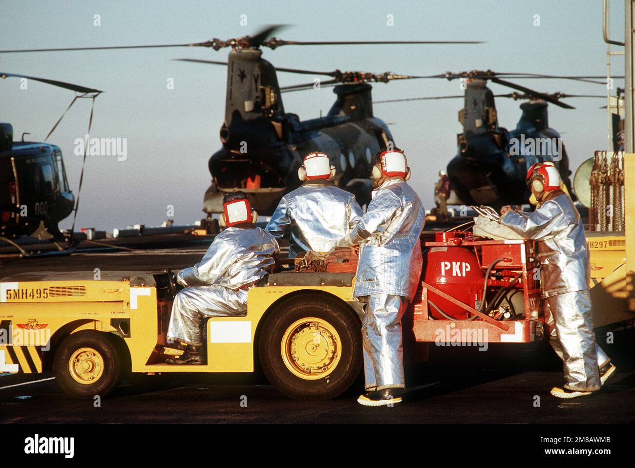 Crash and salvage crewmen wearing proximity suits stand by on the ...