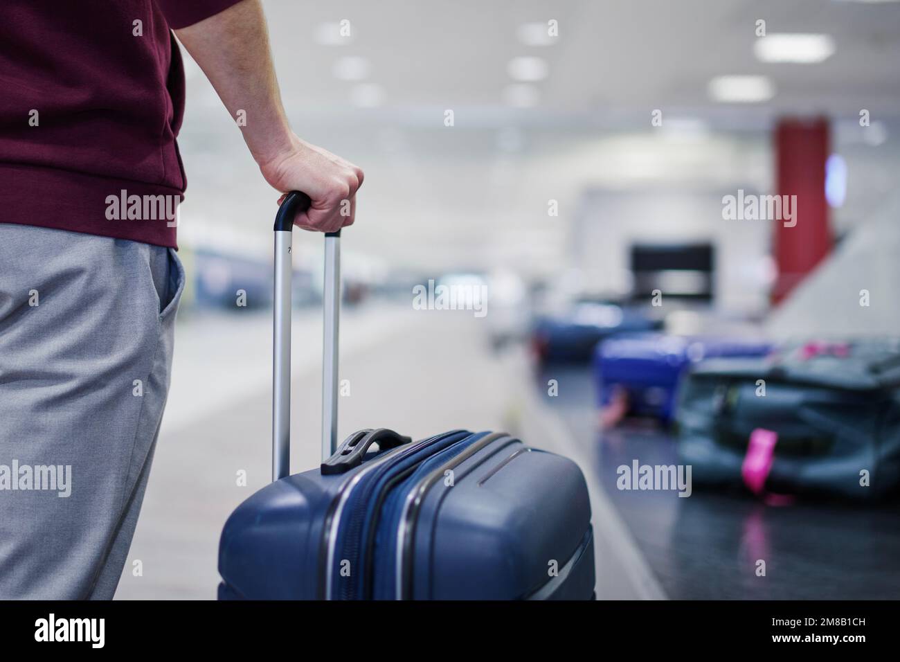 Traveling by airplane. Passenger holding his suitcase in baggage claim ...