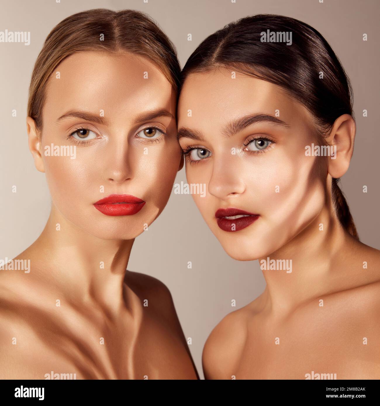 Tender youth. Portrait of two young, beautiful girls with red lips makeup isolated over grey ...