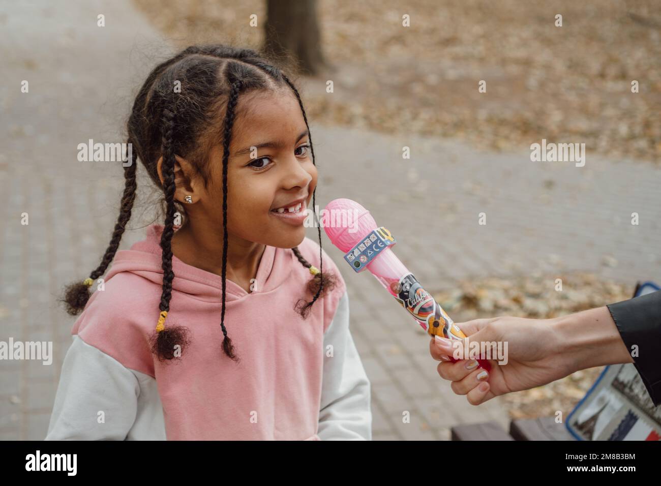 A little girl smiling and talking to a pink microphone-shaped bottle of ...