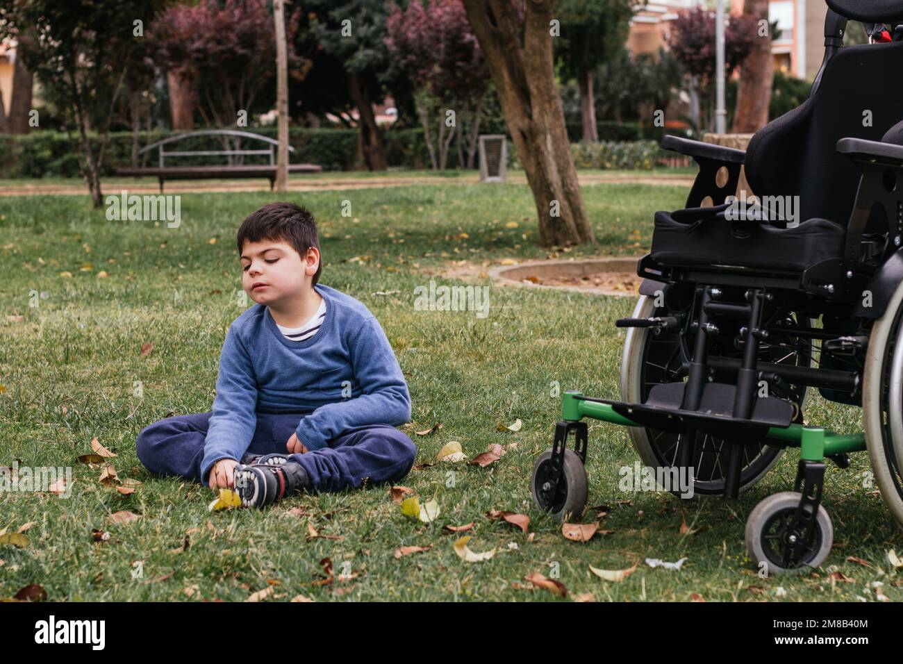 Boy with a disability sitting on a grass in a park with a wheelchair ...