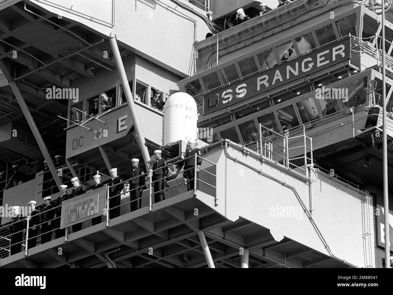 Crew members man the rails beside the island of the aircraft carrier ...