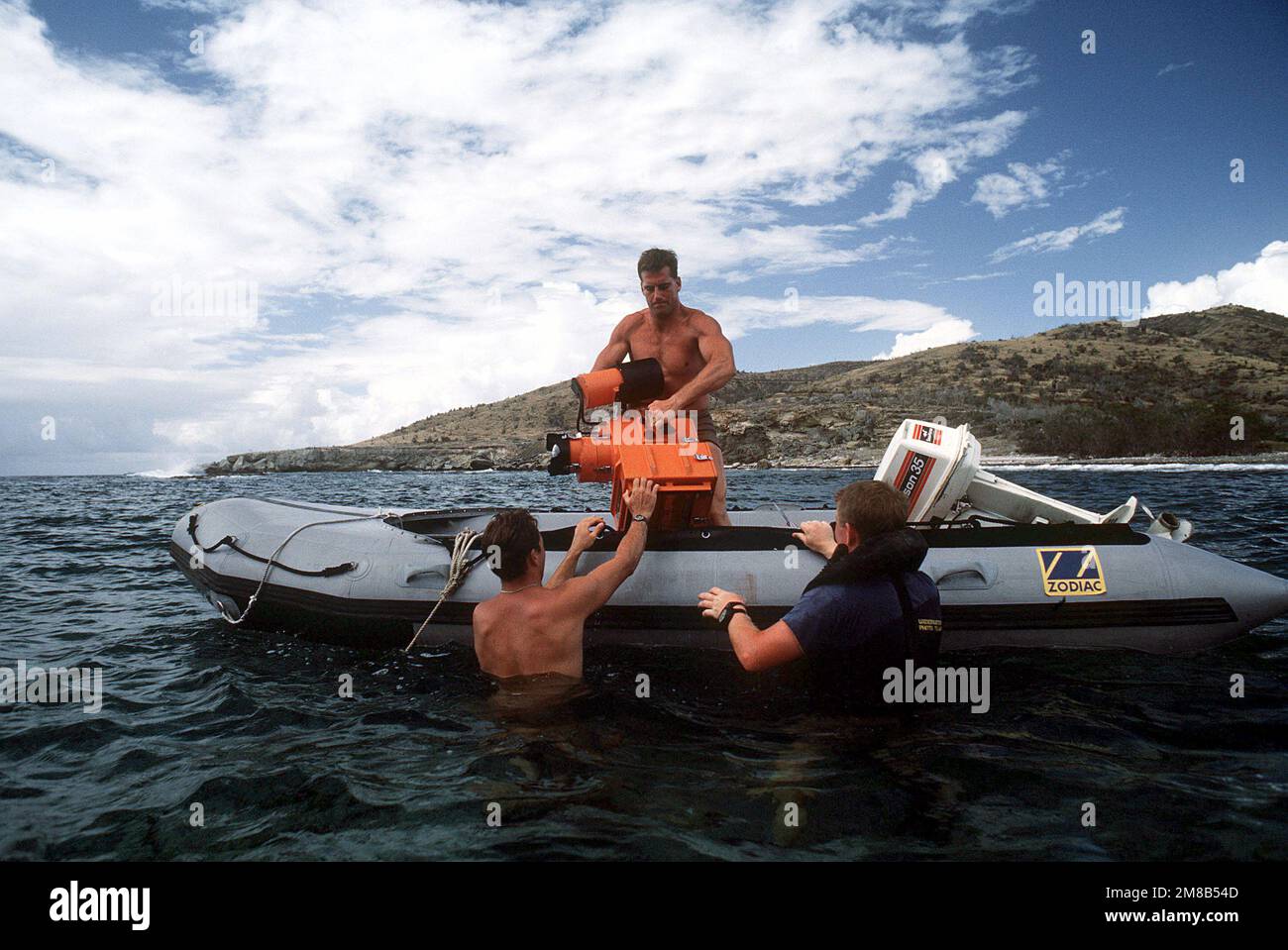 Underwater photographers lift a video camera into their Zodiac raft ...
