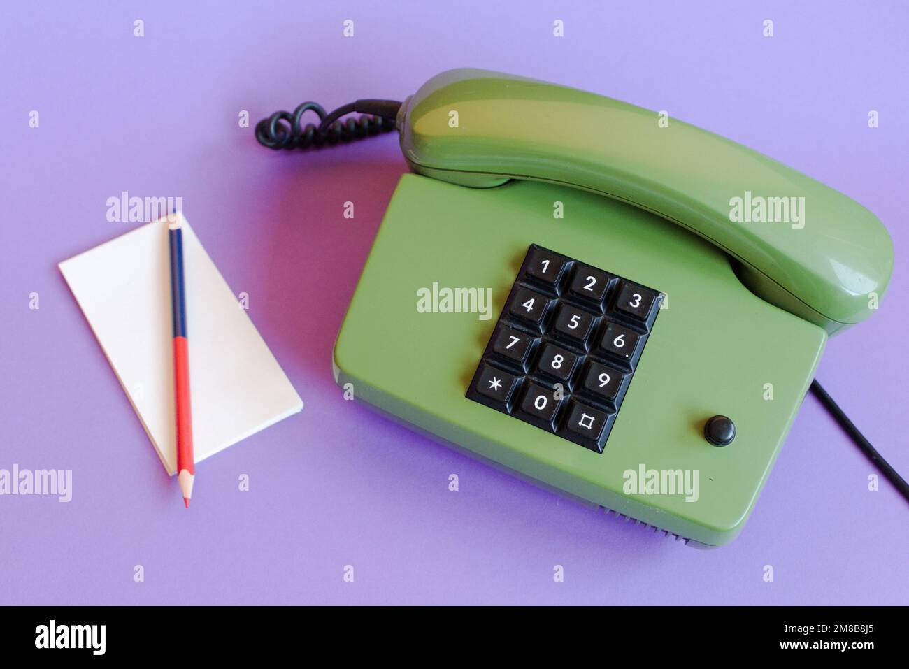 Old green telephone with block notes and pencil on purple background ...