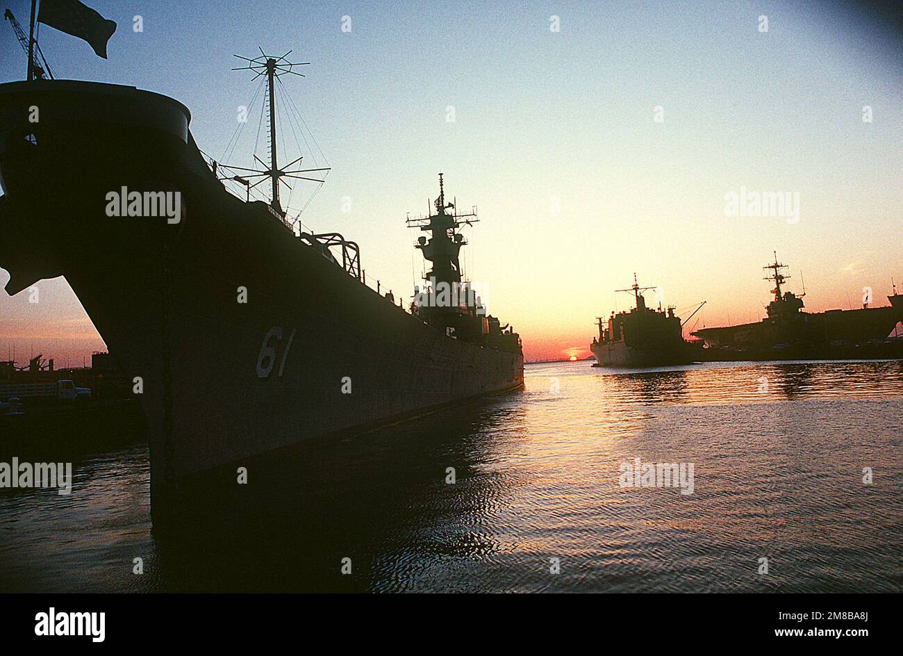 The battleship USS IOWA (BB-61) is silhouetted by the setting sun as it ...