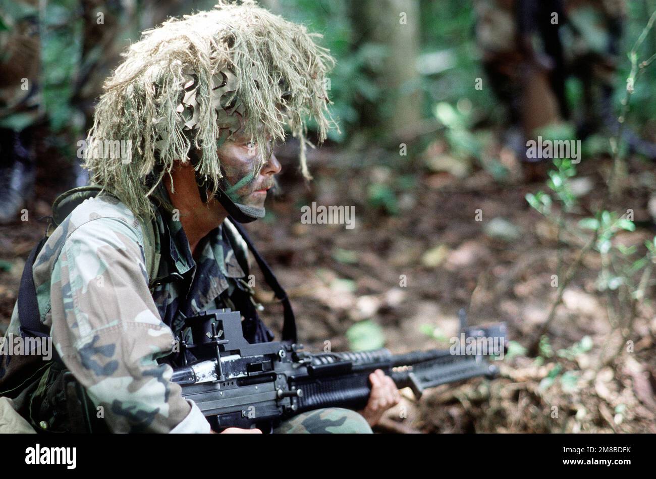 A camouflaged soldier crouches with an M-60 machine gun during jungle ...