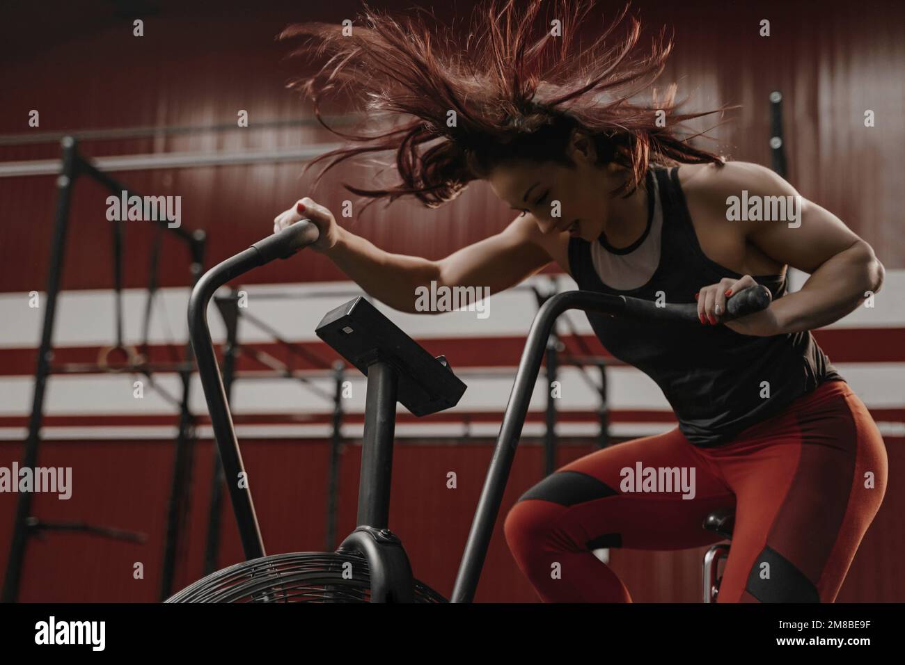 Crossfit woman doing intense cardio training on exercise bike. Her hair ...