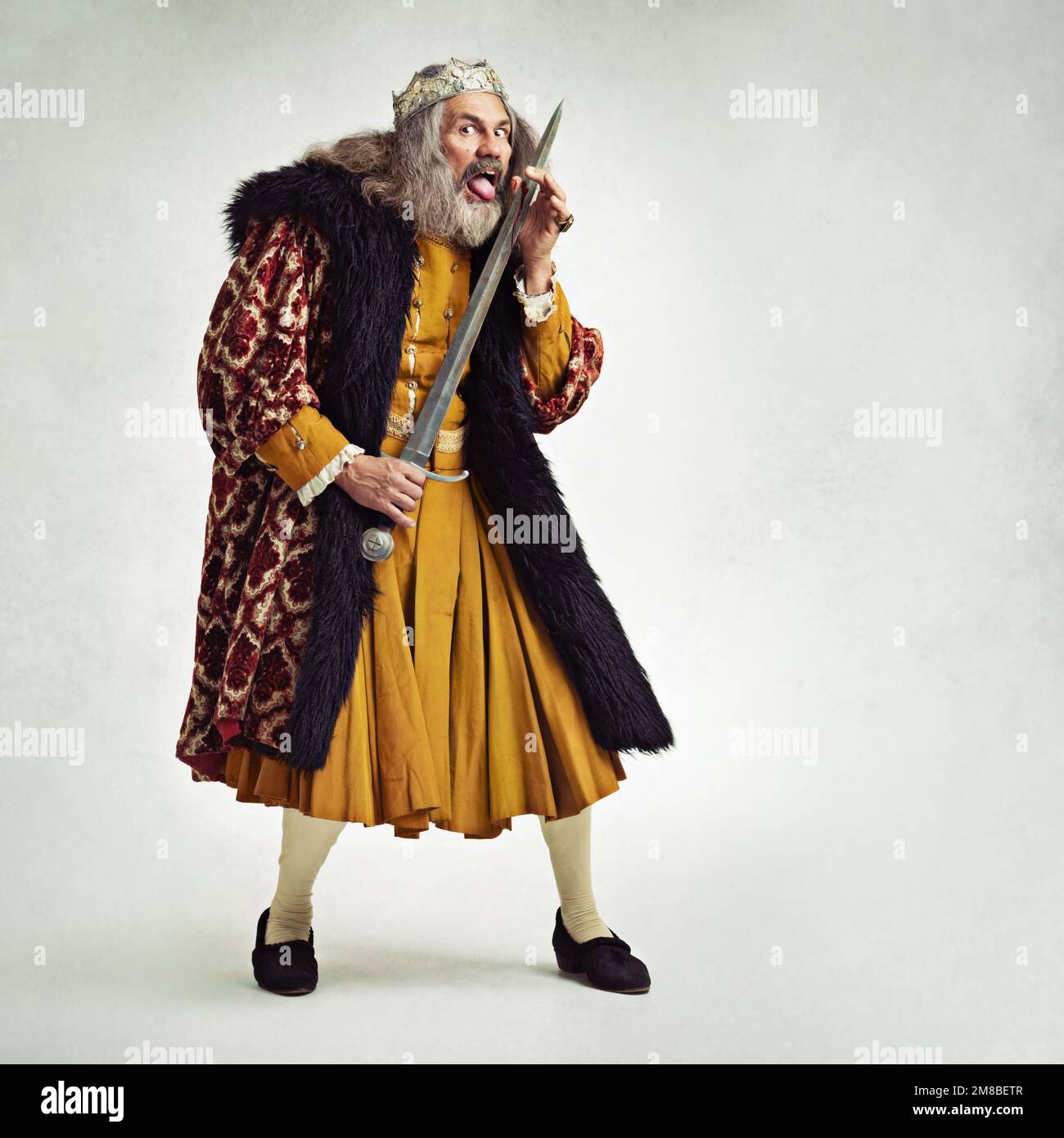 Portrait, king and man lick sword in studio isolated on gray background ...