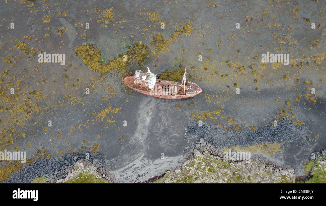 A drone shot of an abandoned ship on mossy green coast island by the ...