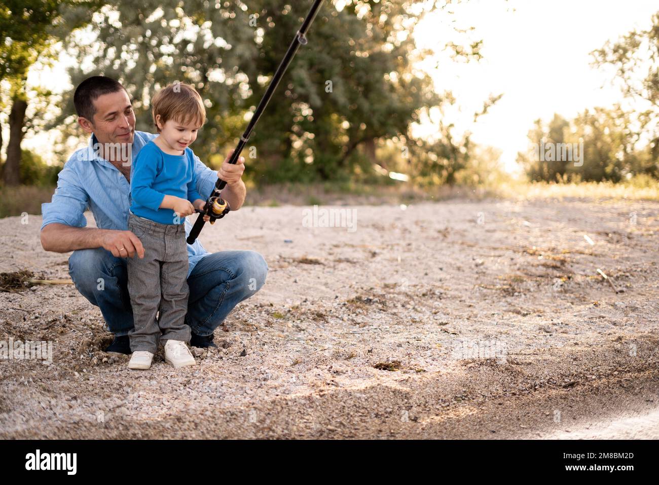 Dad and son fishing together outdoors by a lake. Family leisure concept ...