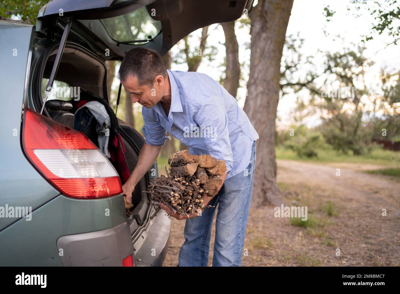 Millennial man getting firewood from car trunk, wooden beams for ...