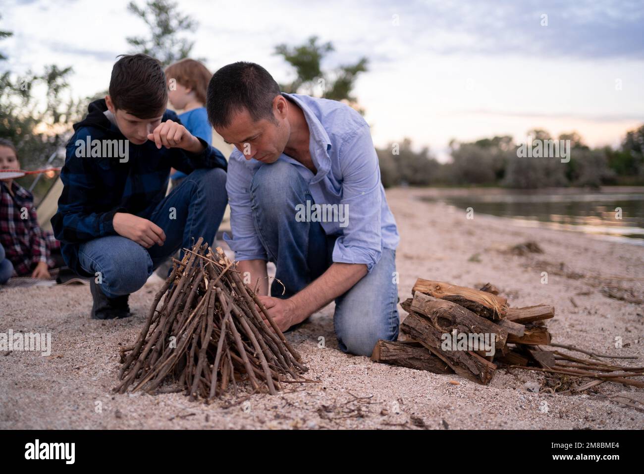 father and son making a campfire in the evening on the shore of the ...