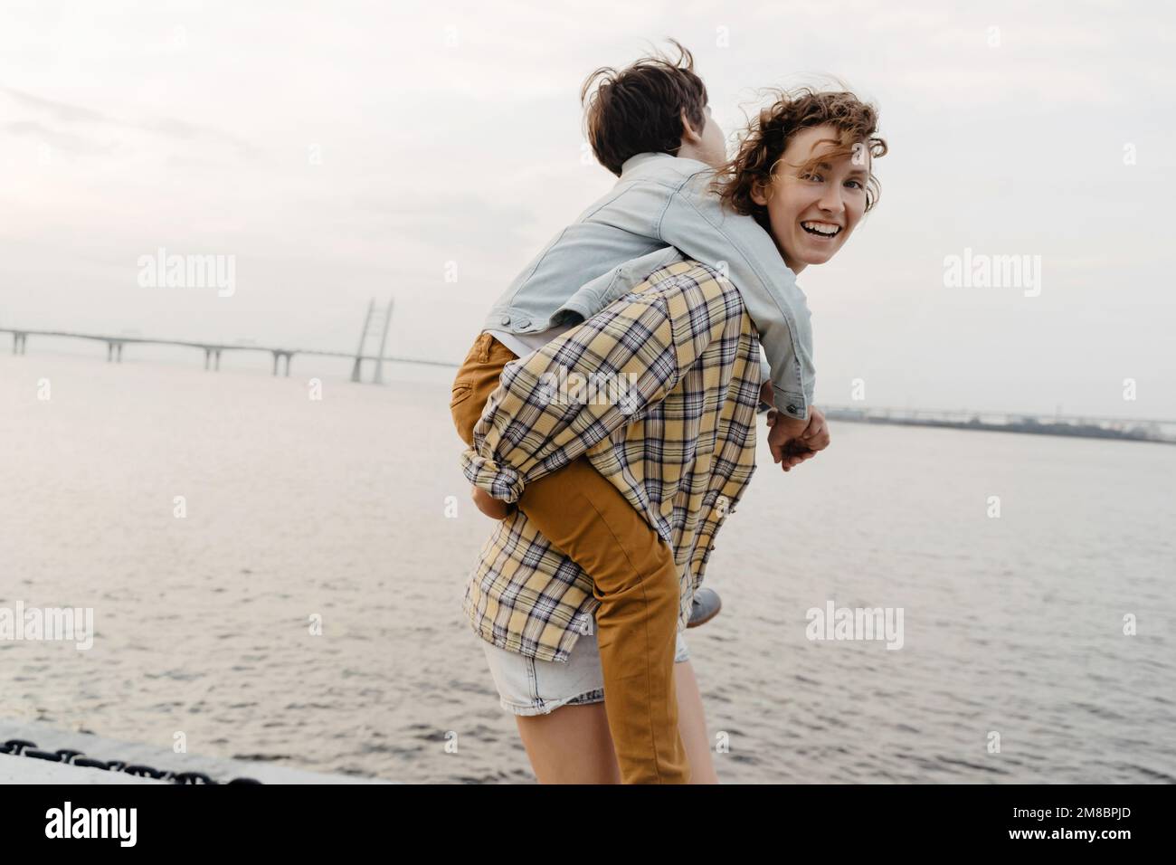 Son enjoying piggyback ride with his young mother while walking. Woman ...
