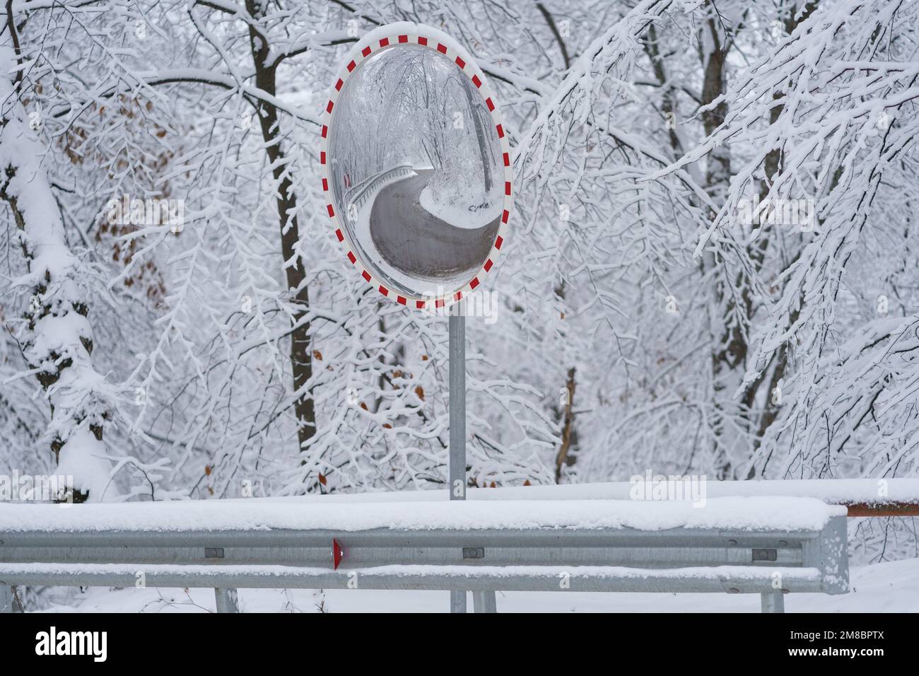 Winter road with mirror installed near sharp turn fenced with iron bump ...
