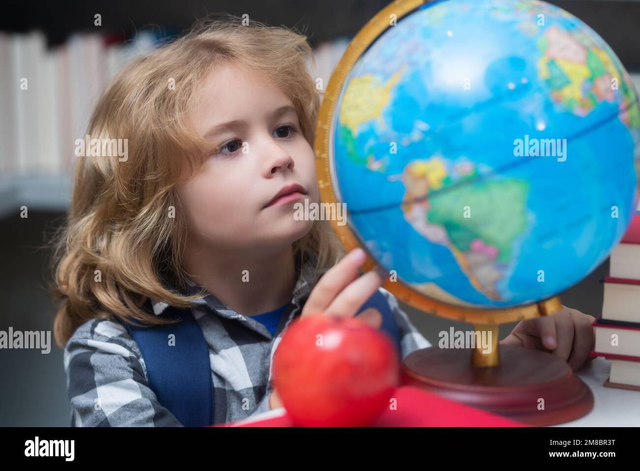 School kid looking at globe in library at the elementary school. Child ...