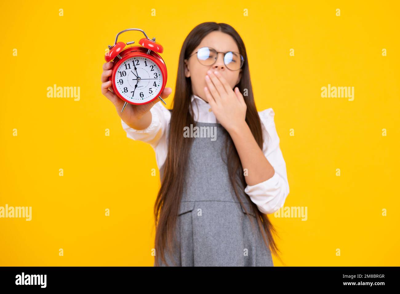 Tired and bored teenager girl child hold clock isolated on yellow ...