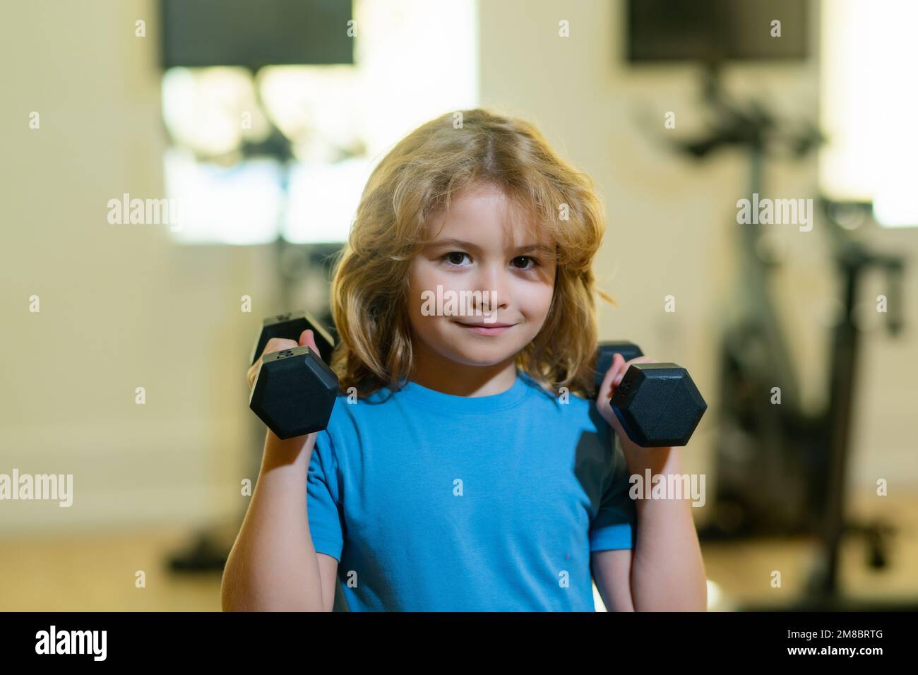 Child boy pumping up biceps muscles with dumbbell. Child workout kid in gym. Fitness kids with ...