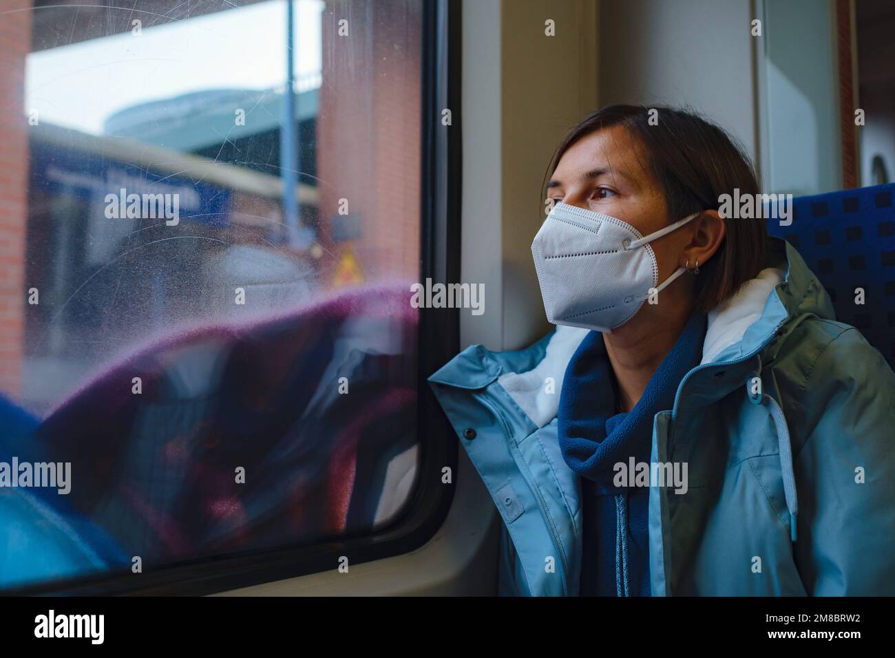 Asian Woman in blue jacket and protective mask looking out of train ...